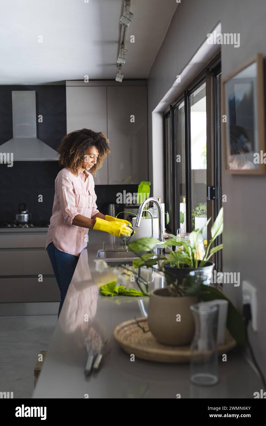 Biracial mother washing dishes at home, with copy space. She's enjoying ...