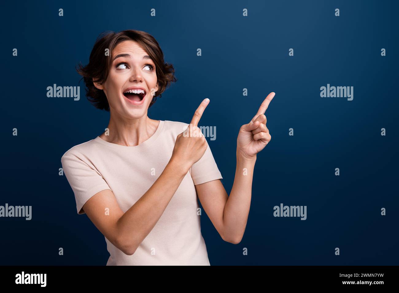 Portrait of funny interested girl directing fingers look blank space ...