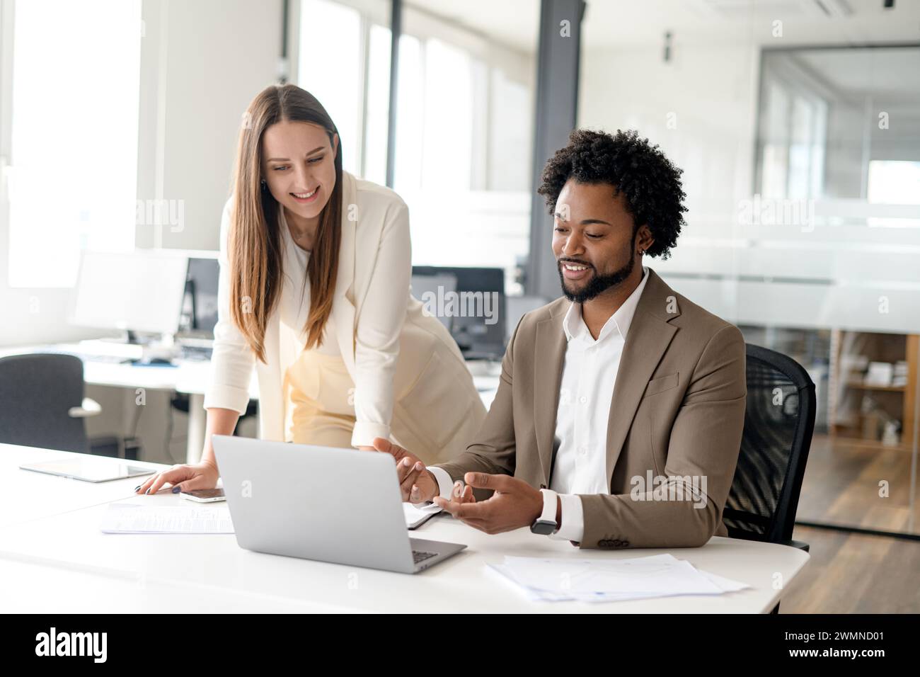 A businesswoman leans over to discuss a point on a laptop with her male ...