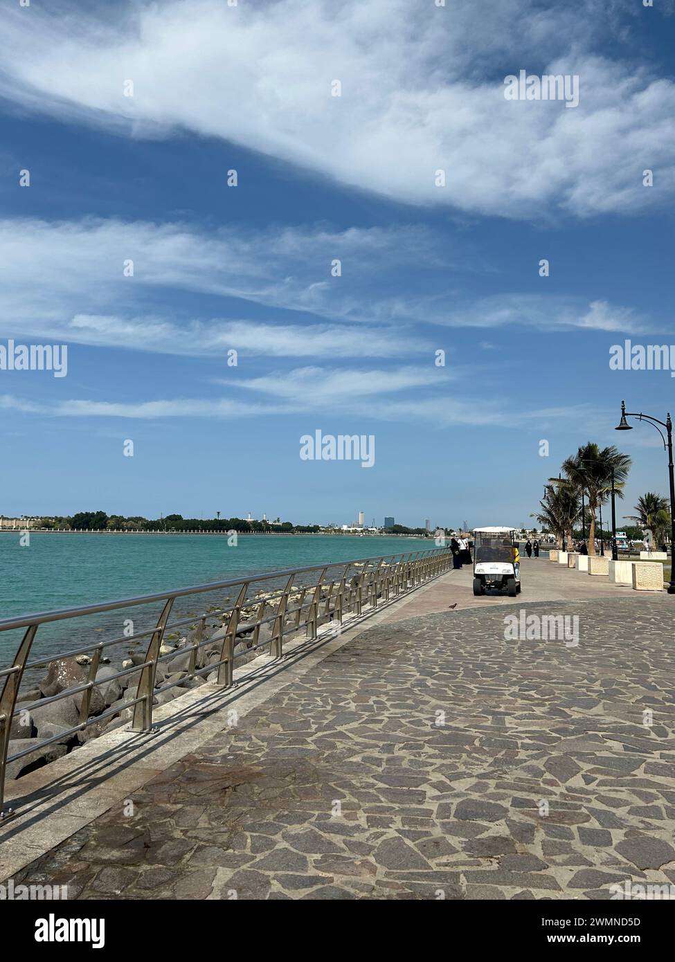 A bench on a seaside walkway with a cityscape backdrop Stock Photo - Alamy