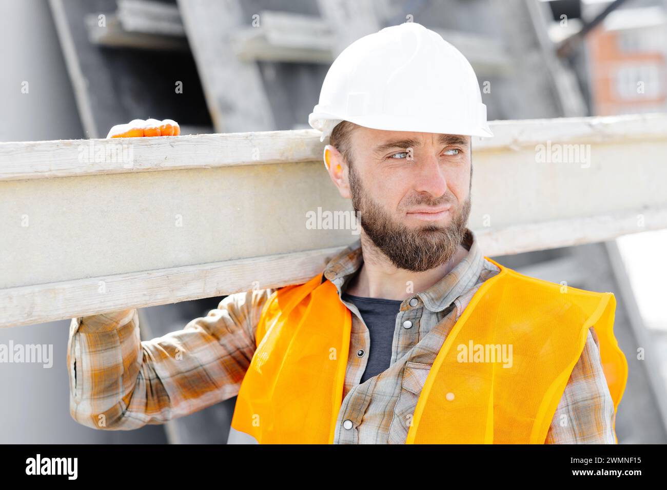 Builder man in hardhat and vest carrying timber on building site in his ...