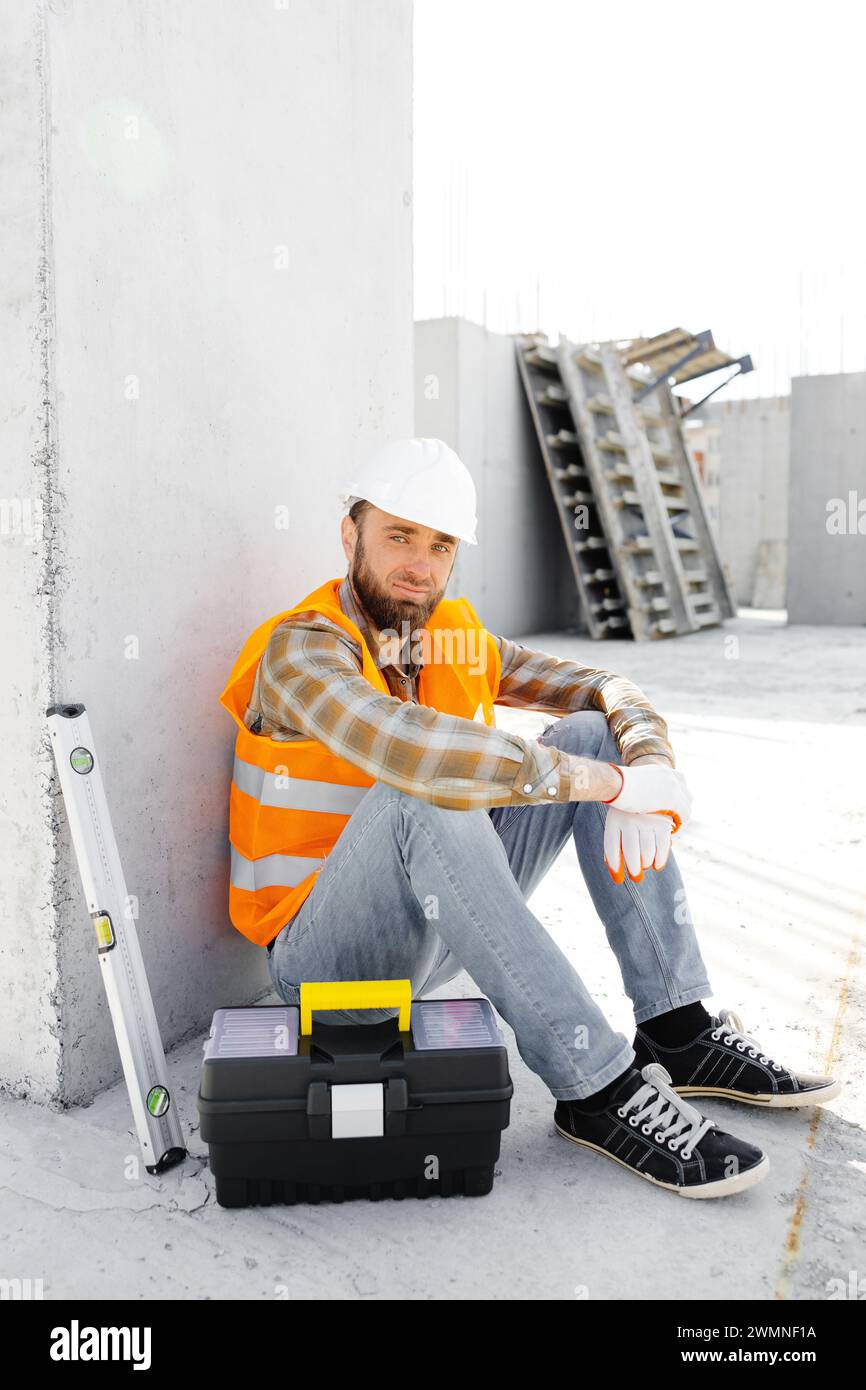 Builder repairman, foreman in safety helmet and vest sitting down to ...