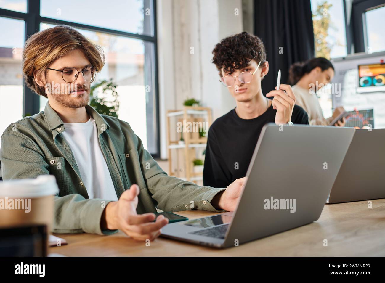 Young startup team deeply focused while working on laptops in modern coworking space, men in 20s ...