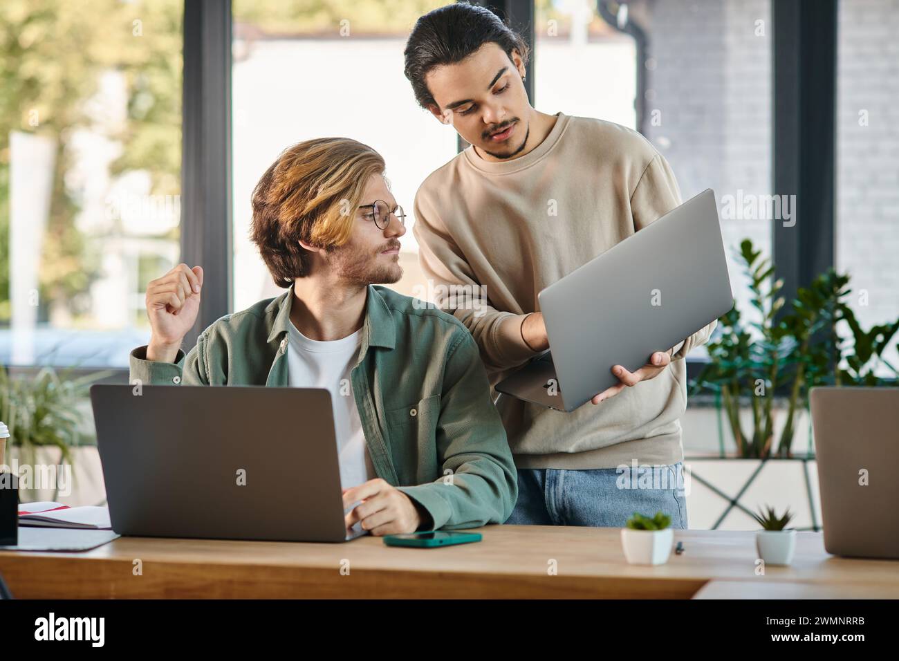 young team lead explain project details to colleague while looking at laptop, men in their 20s ...