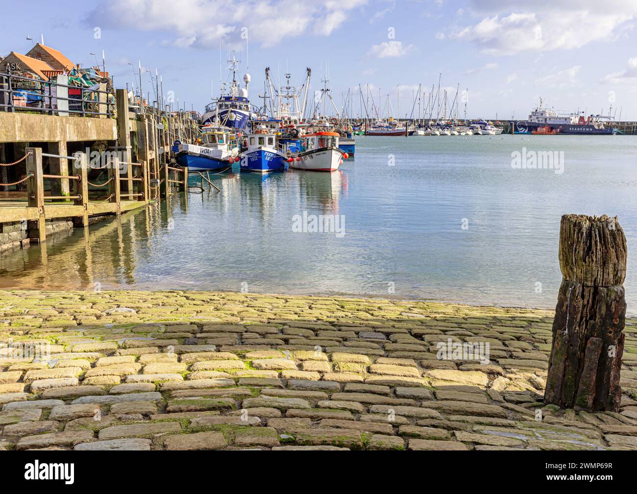 Fishing boats are moored together alongside a quay with a marina in the ...