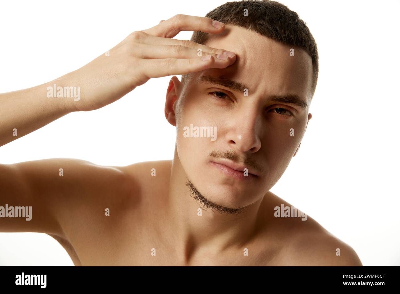 Shirtless young man holding his hand to his forehead and looking to ...