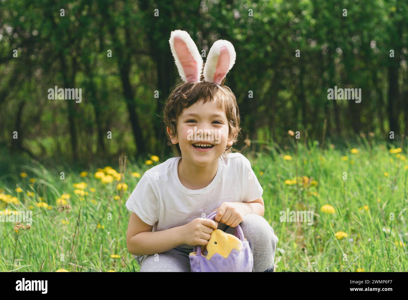 Boy with eggs basket and bunny ears on Easter egg hunt in sunny spring ...