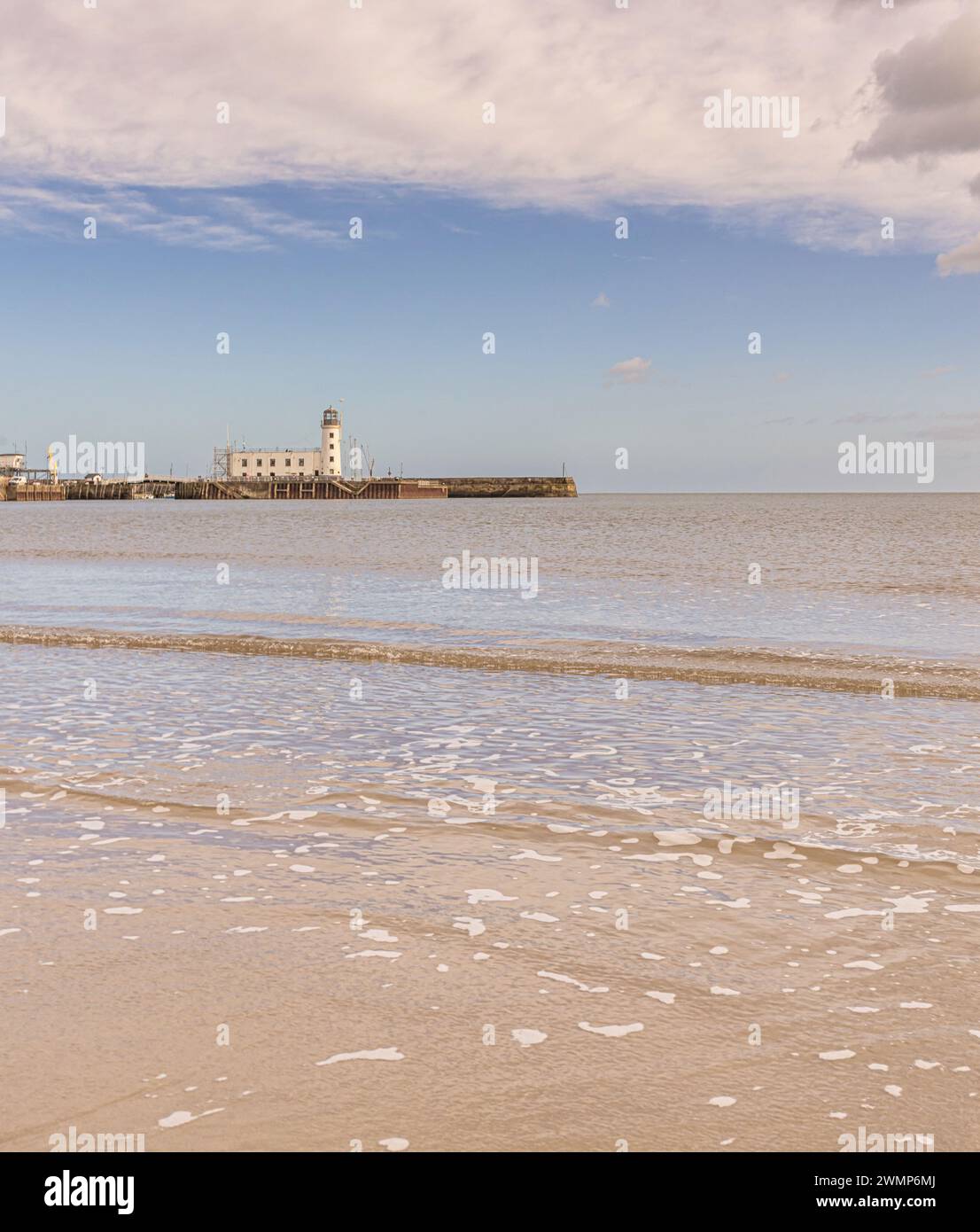 Waves gently roll in towards a beach and a lighthouse stands on a pier ...