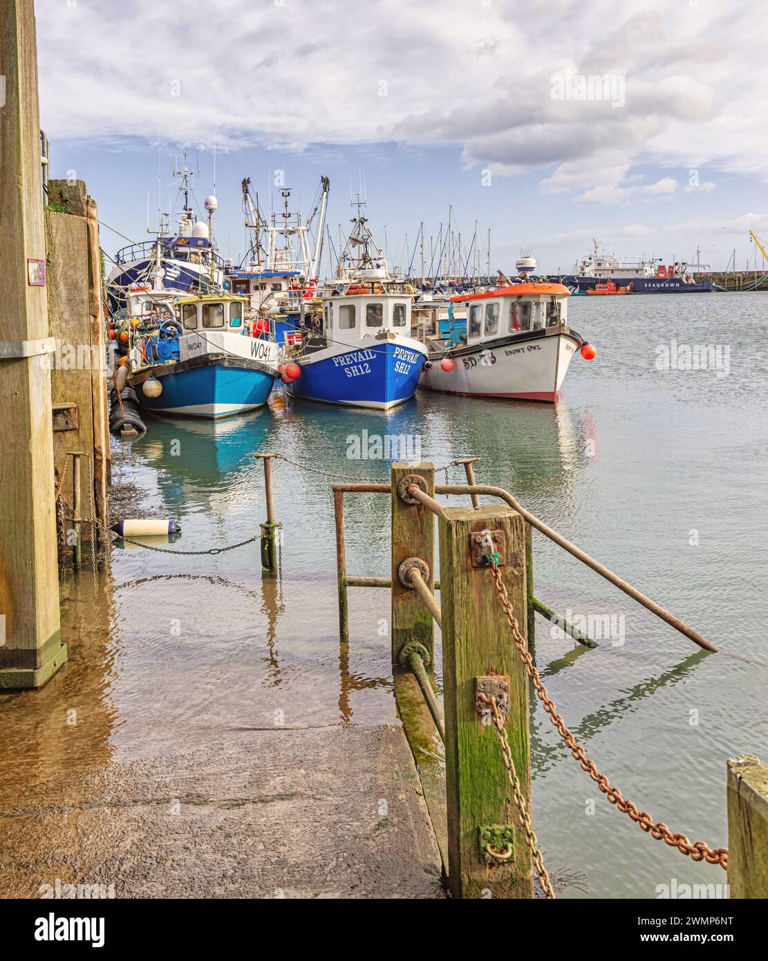 Three fishing boats moored in harbour. A path with wooden posts and ...