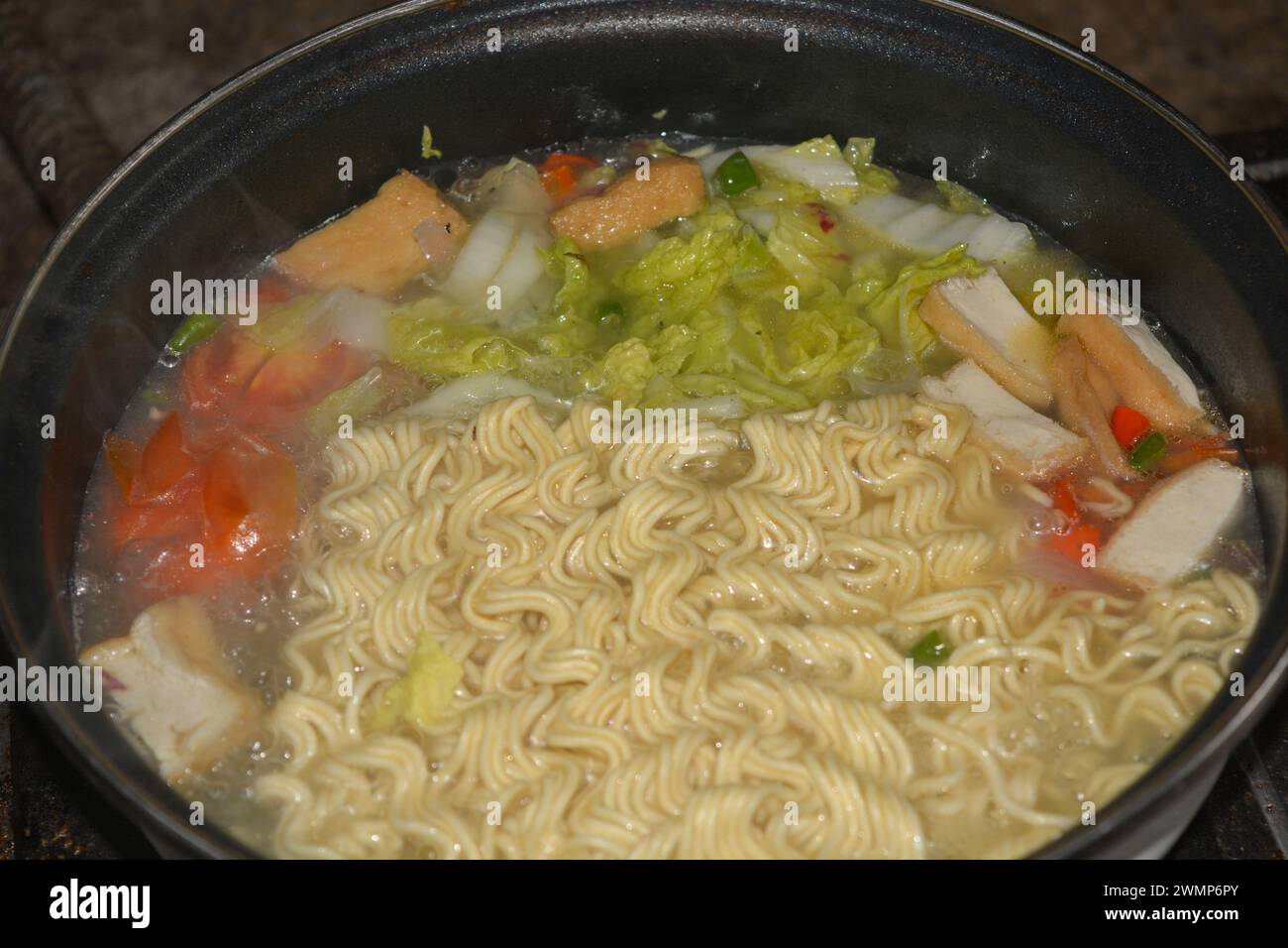 Photo of a pot of noodles being cooked with some vegetable toppings ...