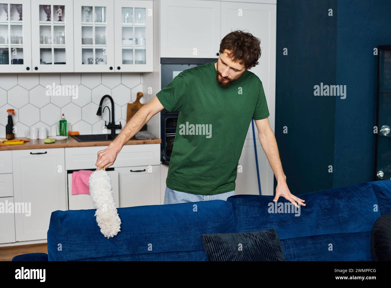 good looking man in comfy casual outfit cleaning sofa with duster with ...
