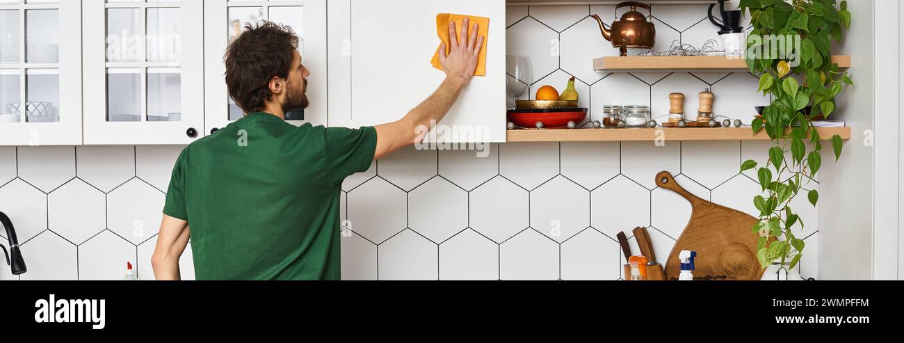 back view of adult man in dark green t shirt using rag to clean kitchen ...