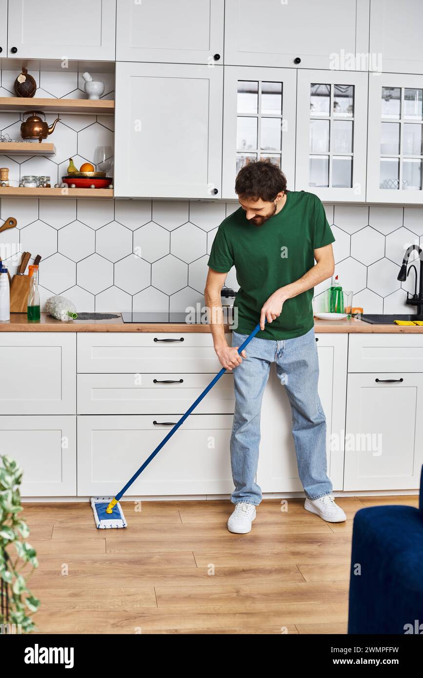 handsome joyous man in comfortable casual attire using mop to clean ...