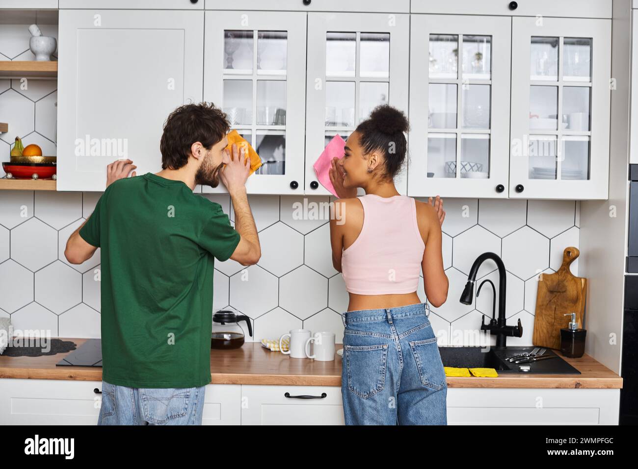 cheerful good looking multiracial couple in homewear using rags to ...