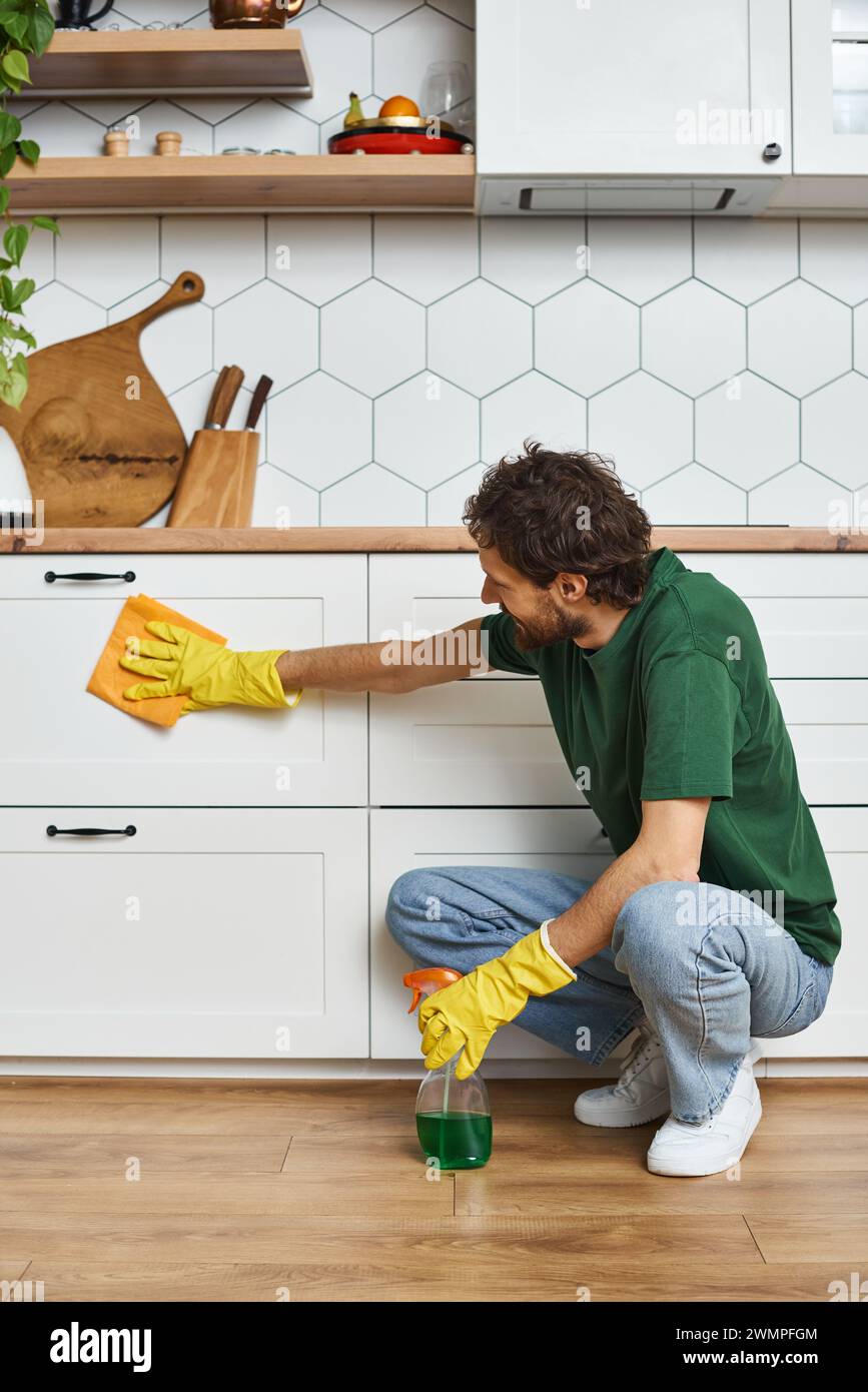 good looking jolly man in casual outfit using rag and cleanser to wash ...