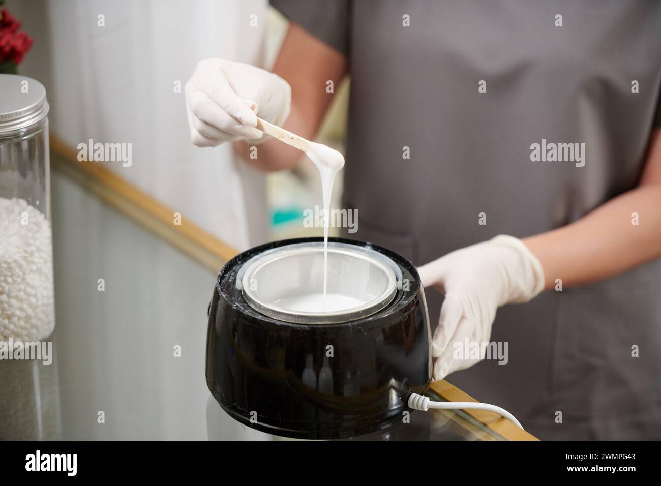 Beautician wearing gloves when mixing melted wax before applying on skin of client Stock Photo ...