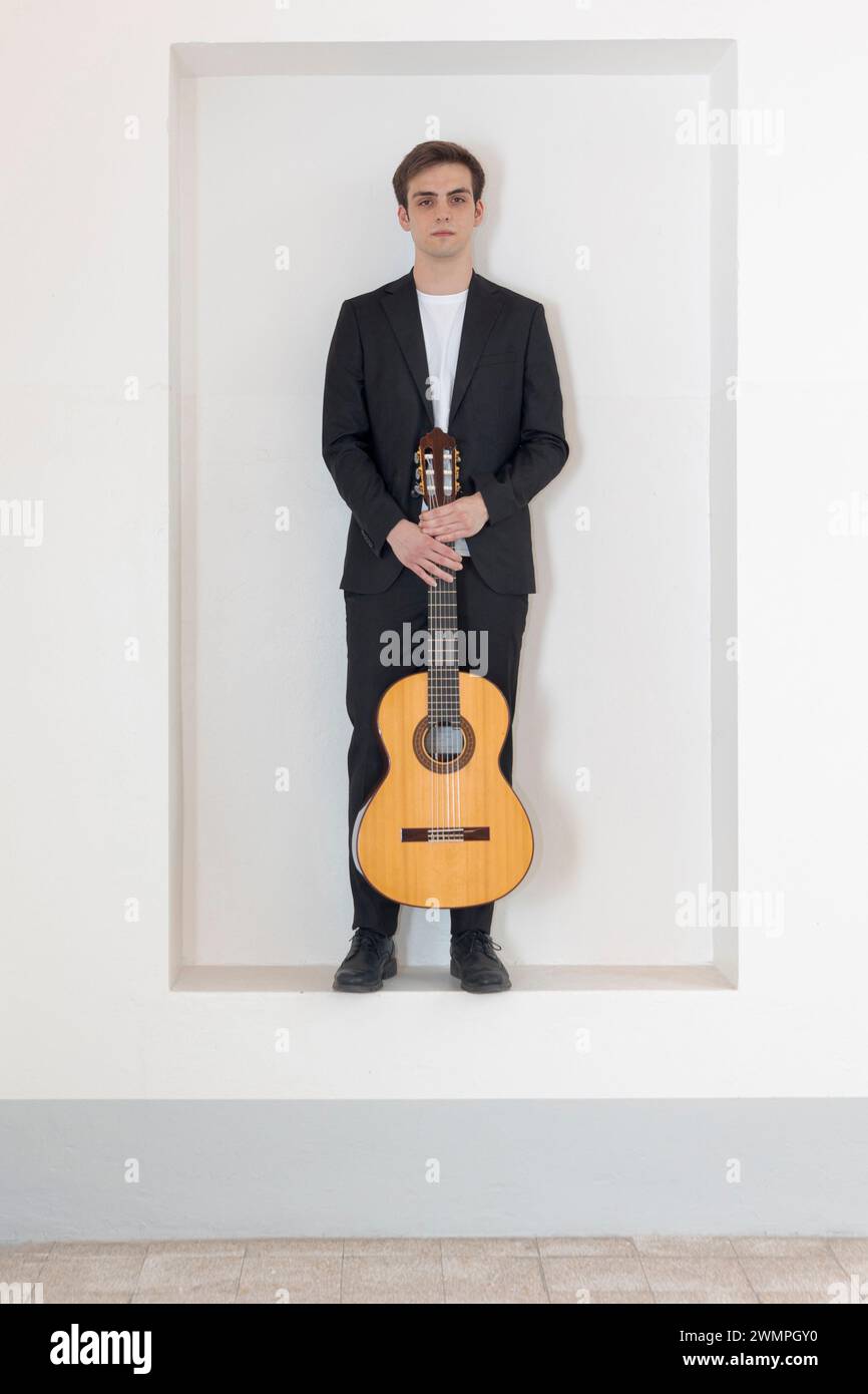 A young boy in an elegant suit stands in a niche in the wall. With both ...