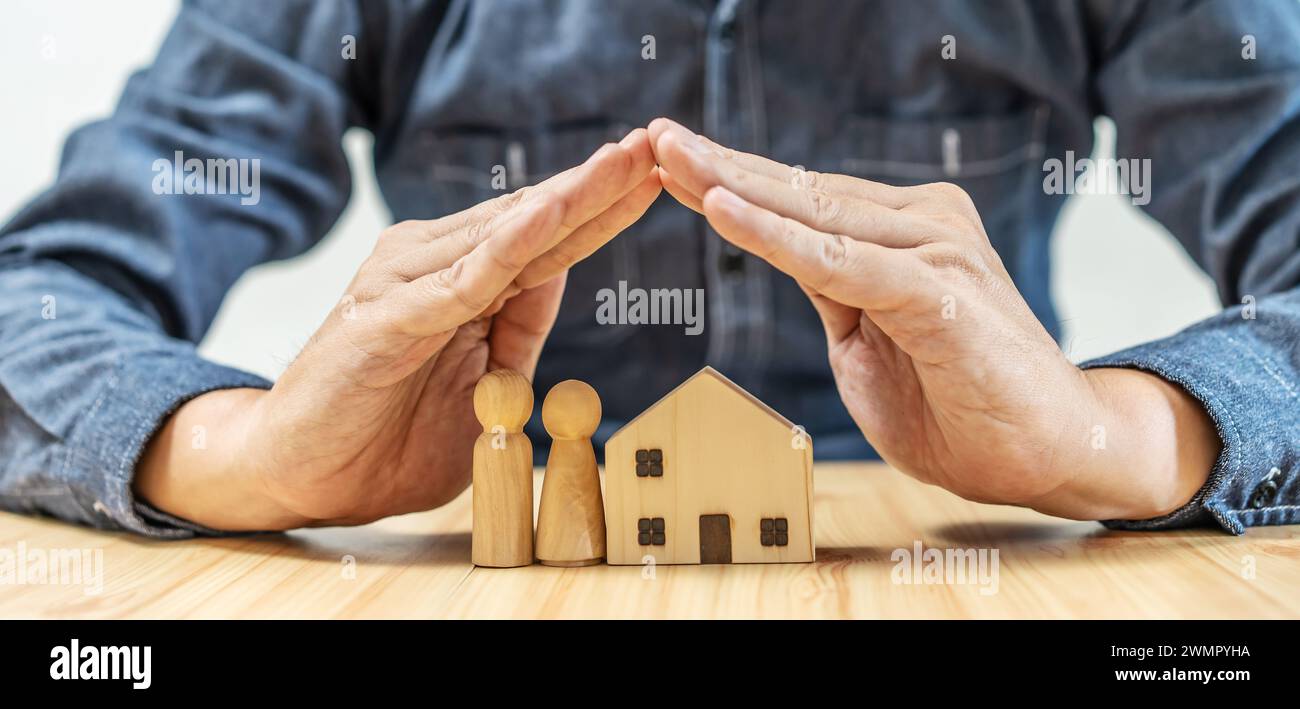 A person showcasing a wooden house and two wooden characters on a table ...