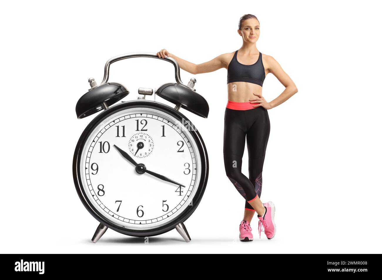 Female fitness trainer leaning on a big alarm clock isolated on white ...