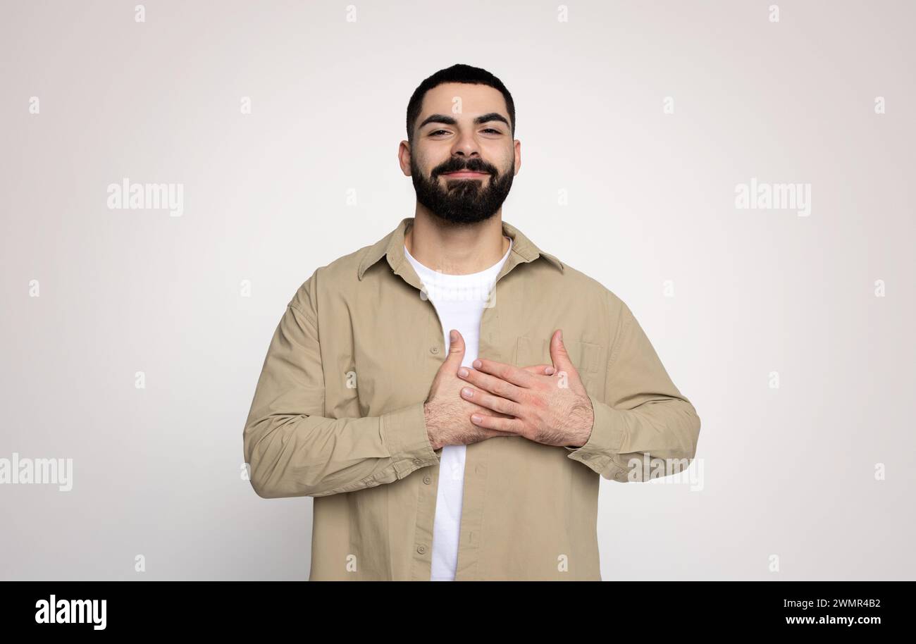 Sincere man with a beard, placing hands on chest in a heartfelt gesture ...