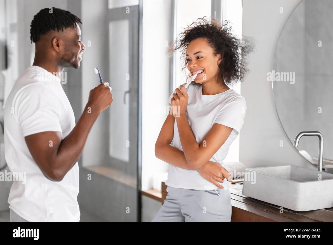 Young African American couple stands together brushing teeth at ...