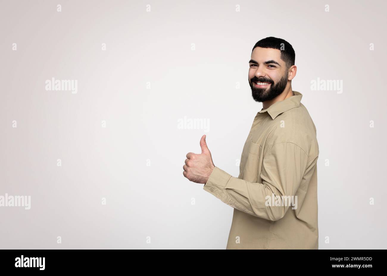 Side profile of a smiling bearded man in a beige shirt giving a thumbs ...