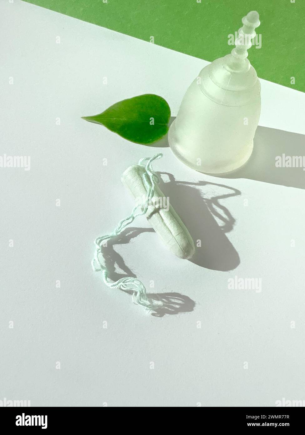 A reusable silicone menstrual cup and standard tampon on white and ...