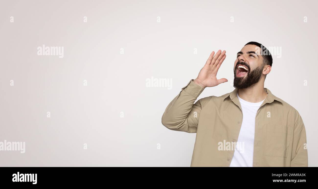 Exuberant bearded man shouting to the side with hand cupped to his ...
