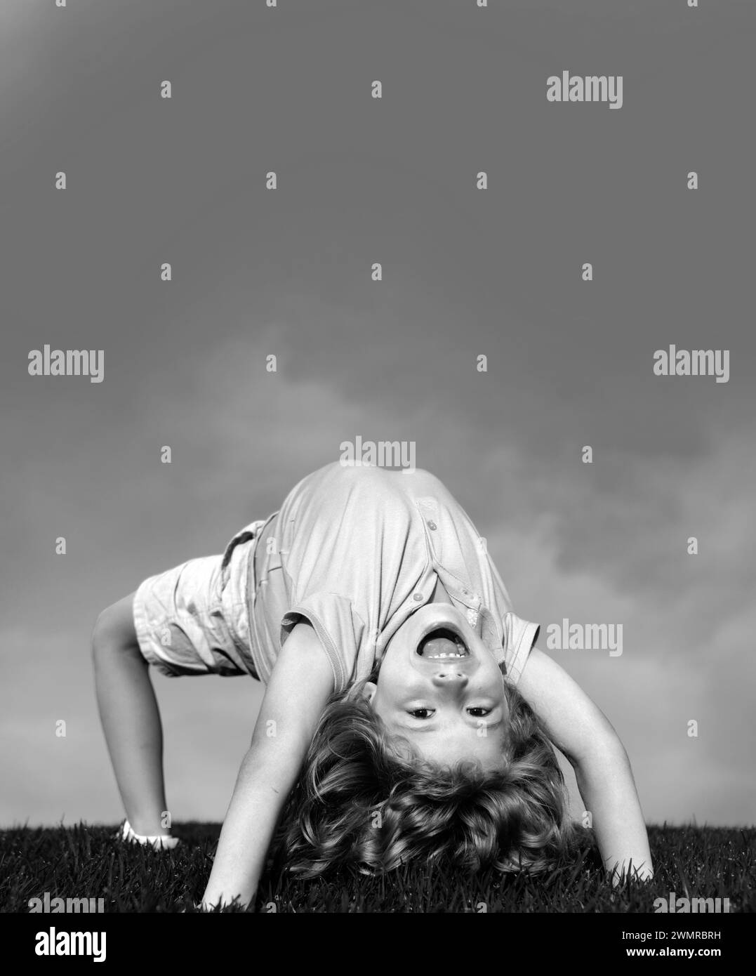 Happy child standing upside down on green grass. Laughing kid boy ...