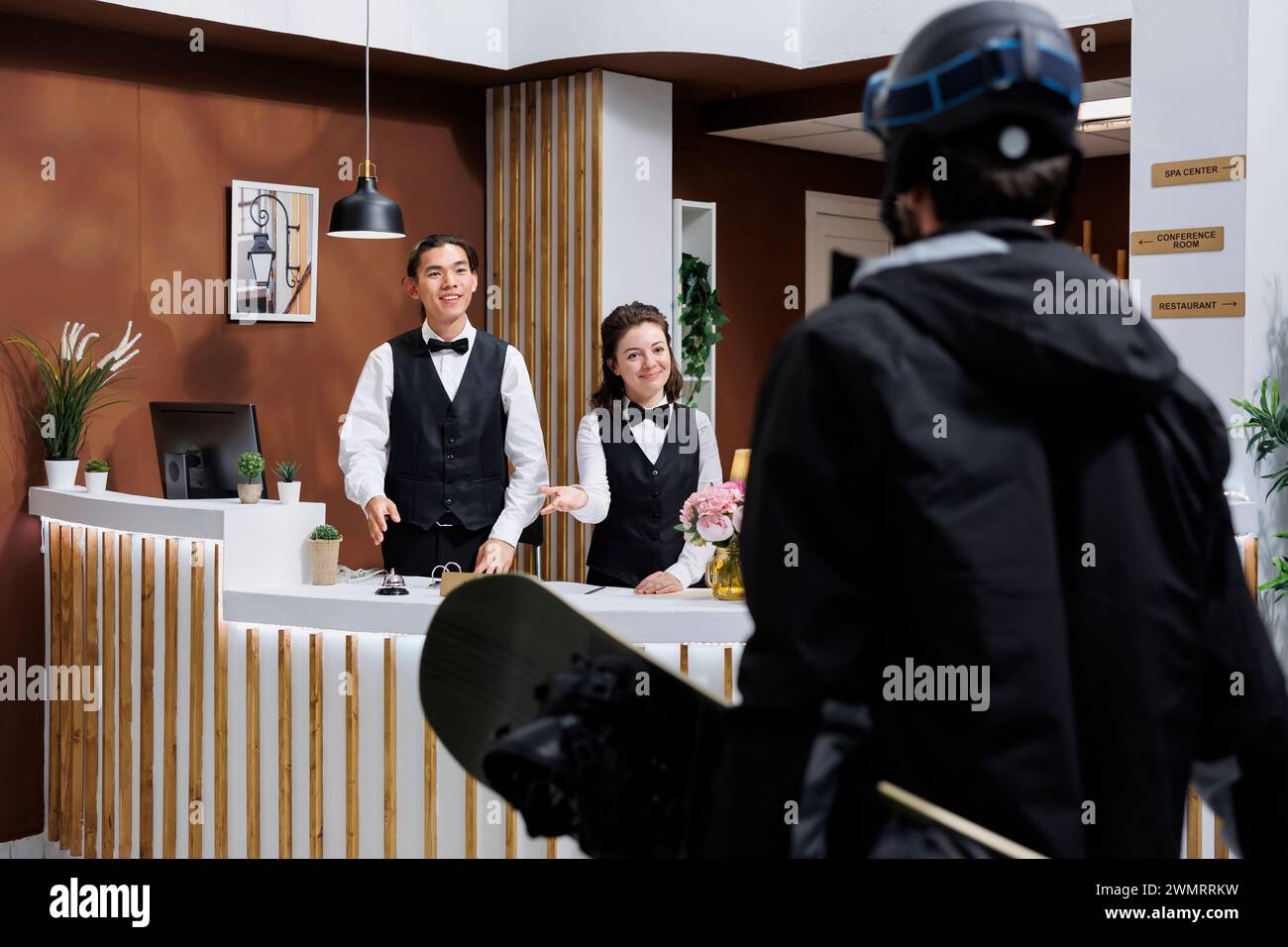 At front desk of exclusive winter resort, two receptionists warmly ...