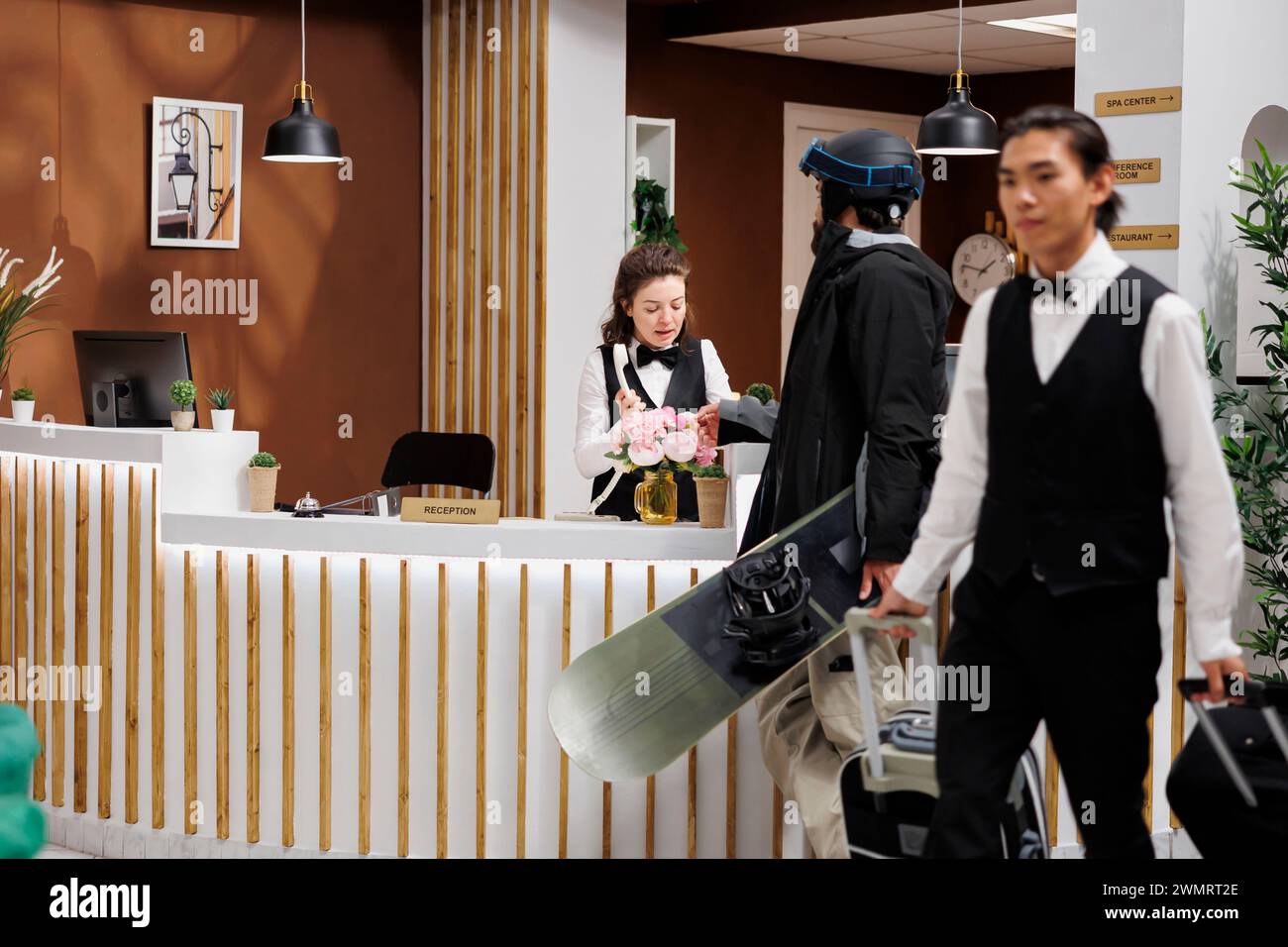 Female receptionist at front desk assists man with snowboarding ...