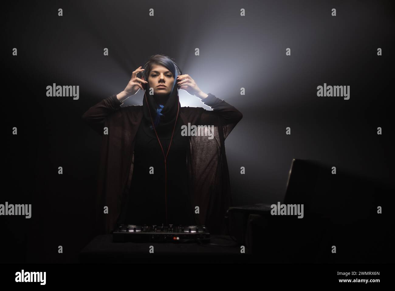 Woman holding headphones and operating DJ mixer inside a dark room ...