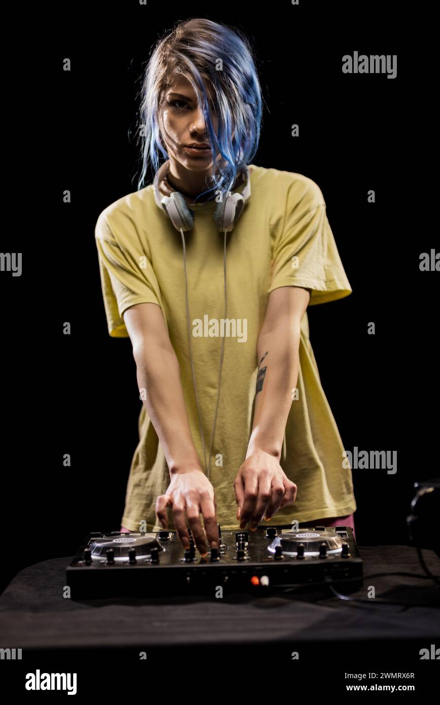 Girl wearing headphones is focused on mixing music on a soundboard ...
