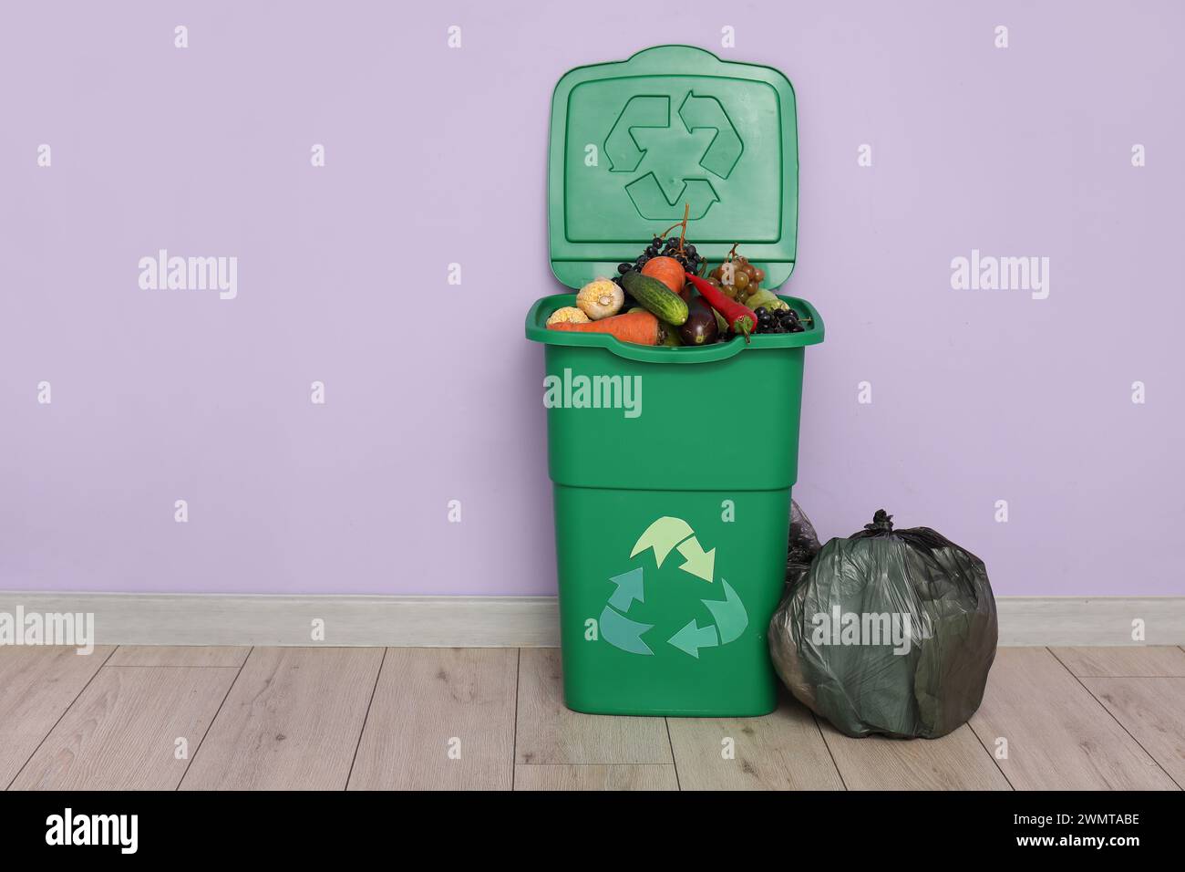 Container for trash with food waste and full garbage bags near lilac ...