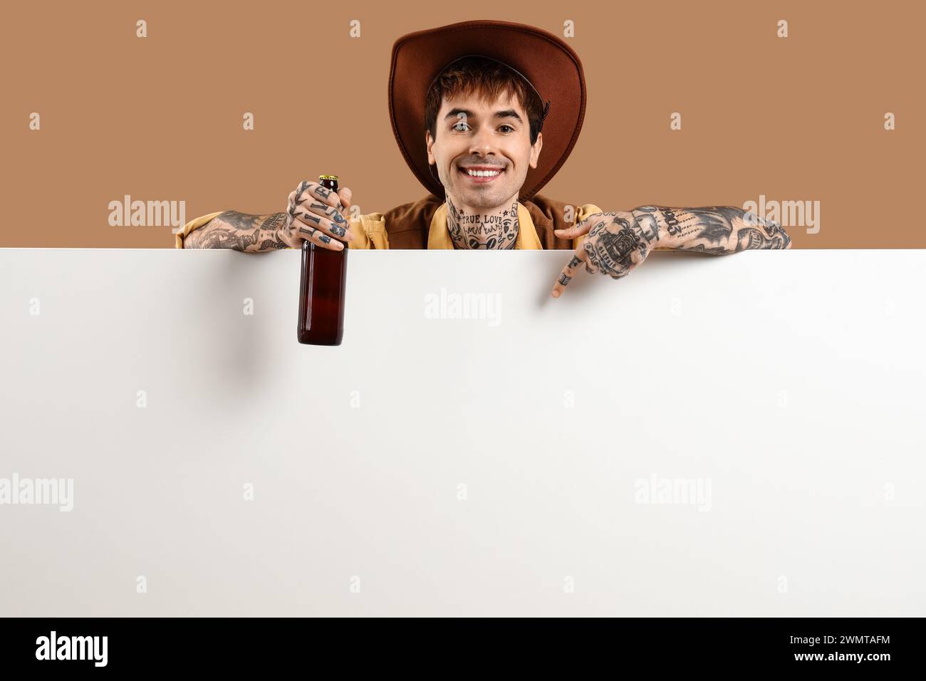 Male bartender dressed as cowboy with bottle of beer pointing at blank ...