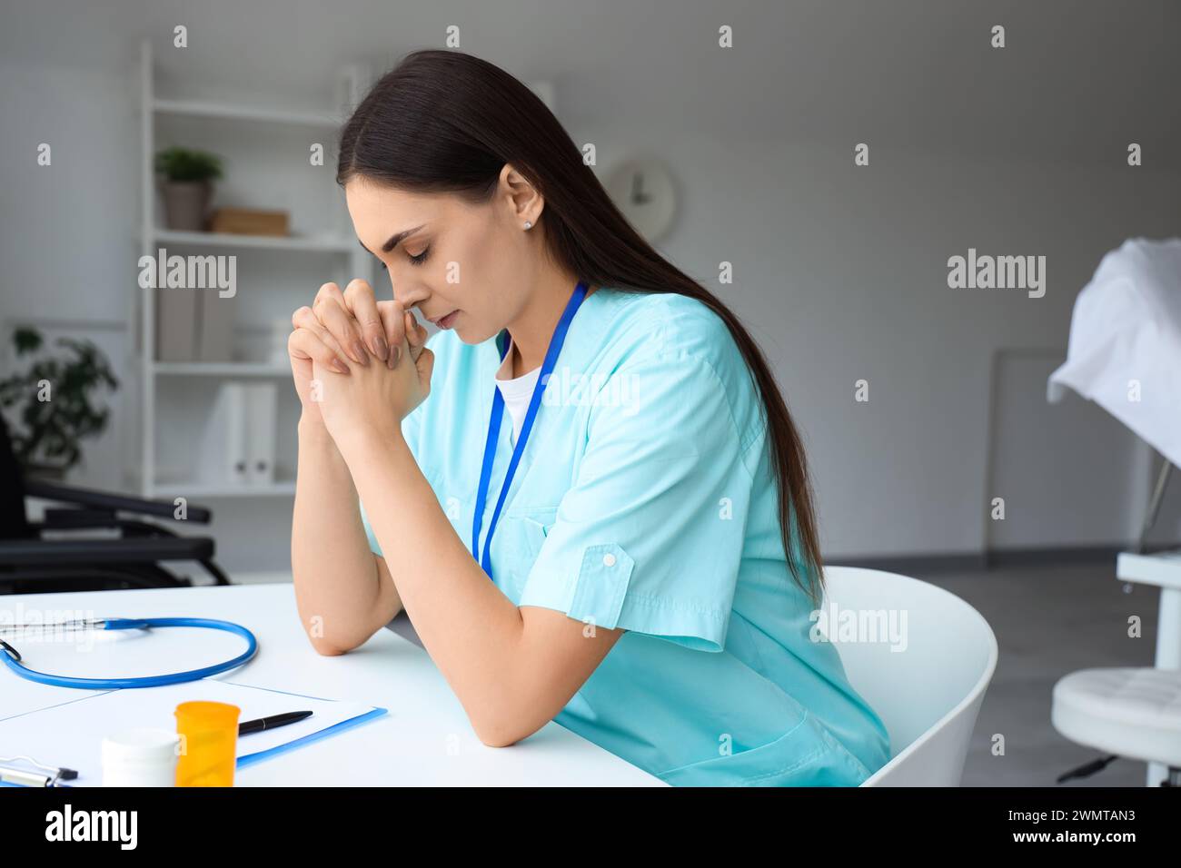 Female nurse praying at table in clinic Stock Photo - Alamy