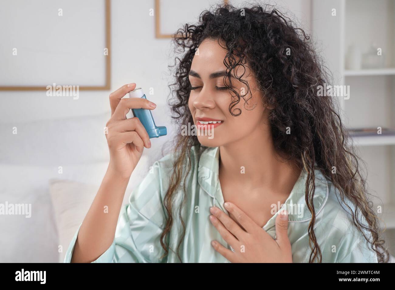 Happy young African-American woman with asthma inhaler in bedroom ...