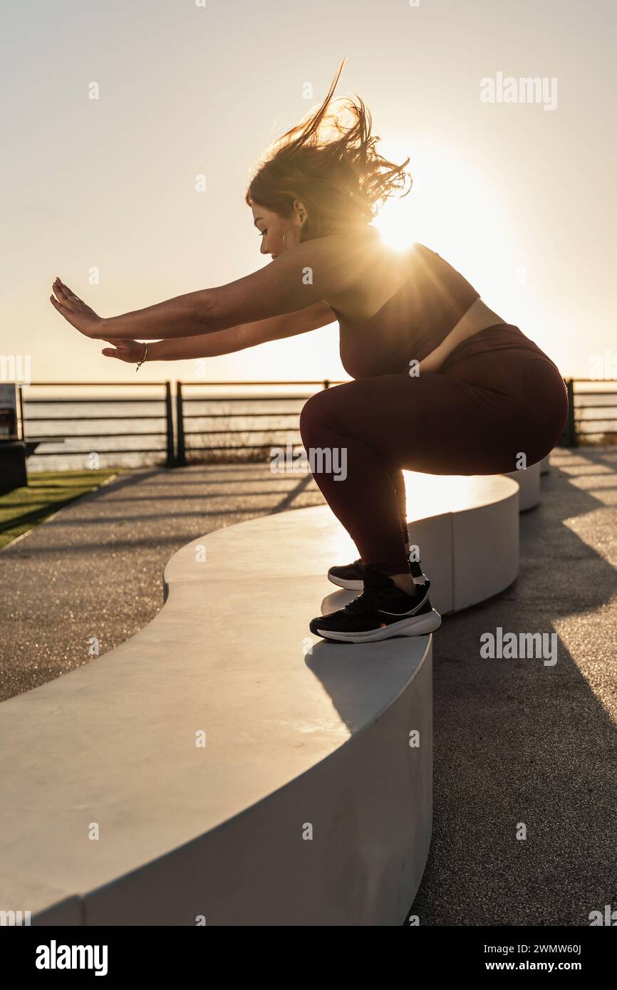 Active woman in a deep squat against the sunrise - Embracing a healthy ...