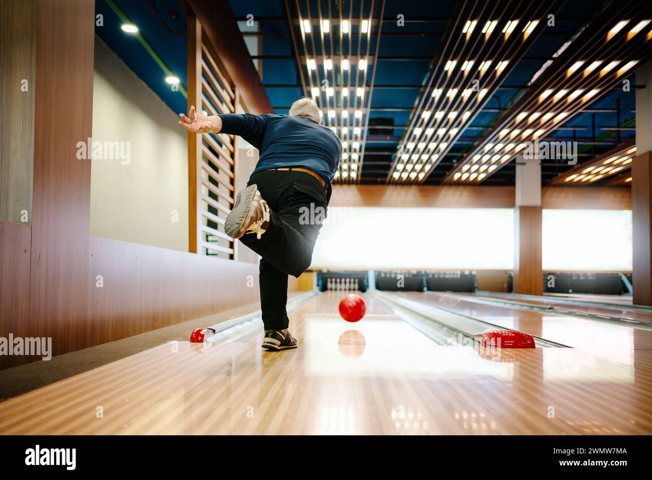 Senior man with throwing bowling ball, captured in modern bowling alley ...