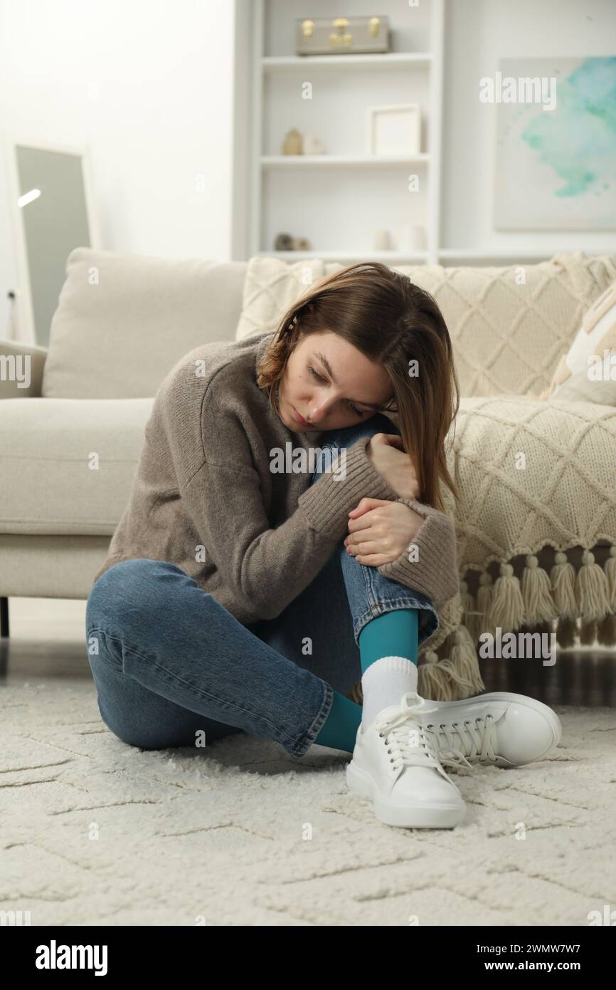 Sad young woman sitting on floor at home Stock Photo - Alamy