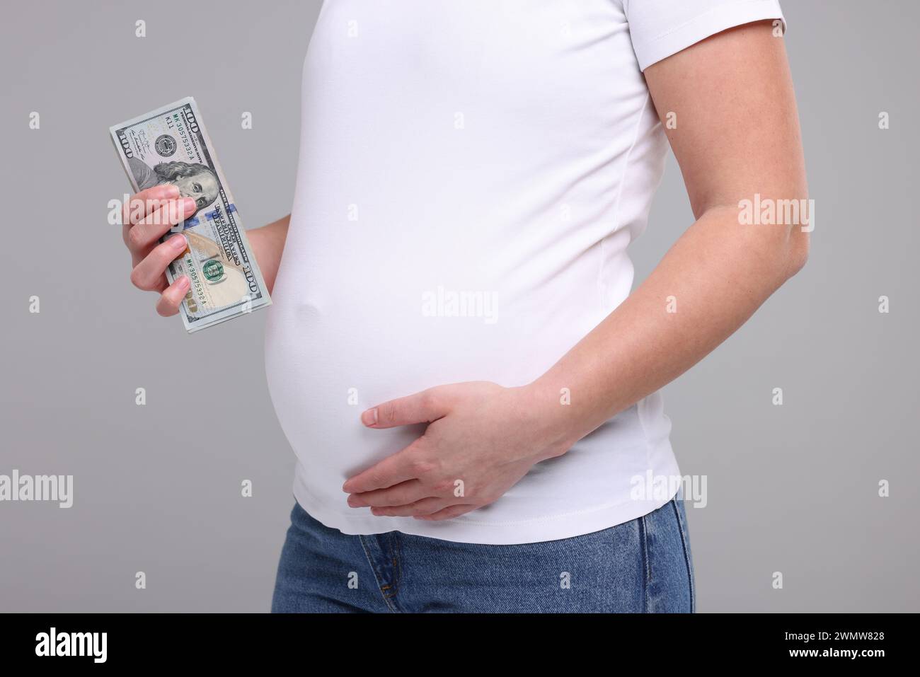 Surrogate mother. Pregnant woman with dollar banknotes on light grey ...