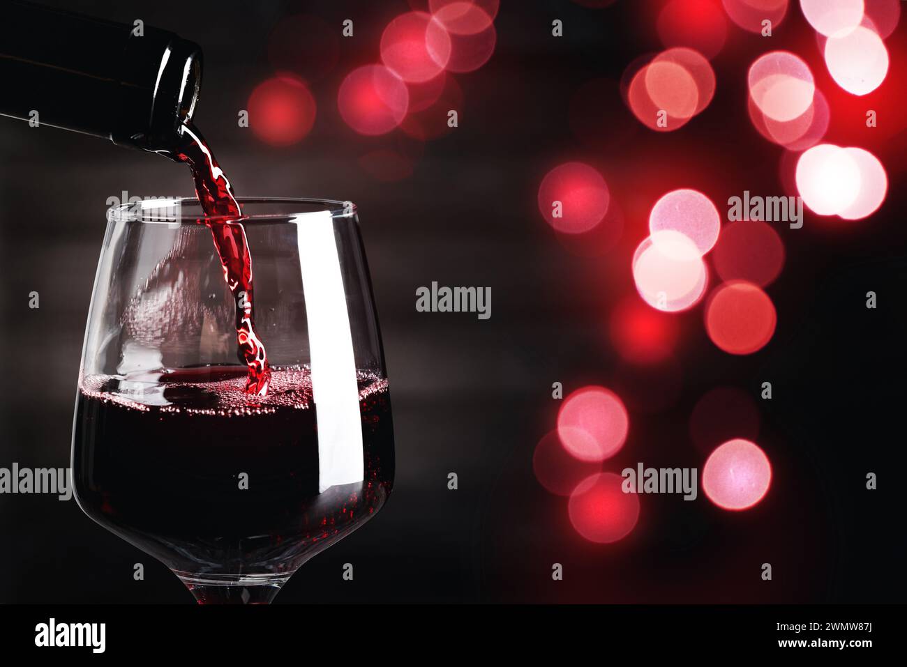 Pouring red wine into glass against dark background with blurred lights, closeup. Space for text ...