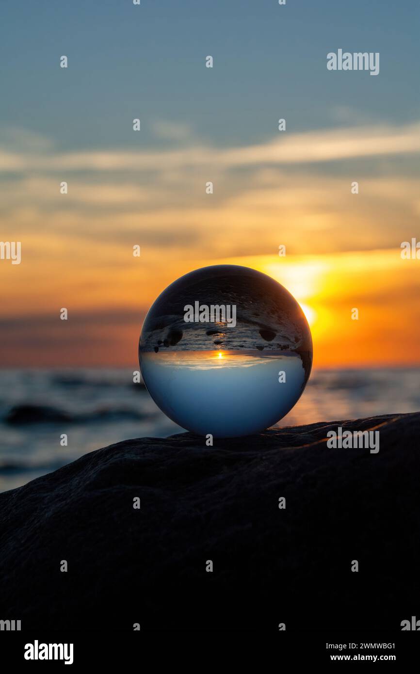 Glass ball on a rock at sunset on the beach, the sea and the setting ...