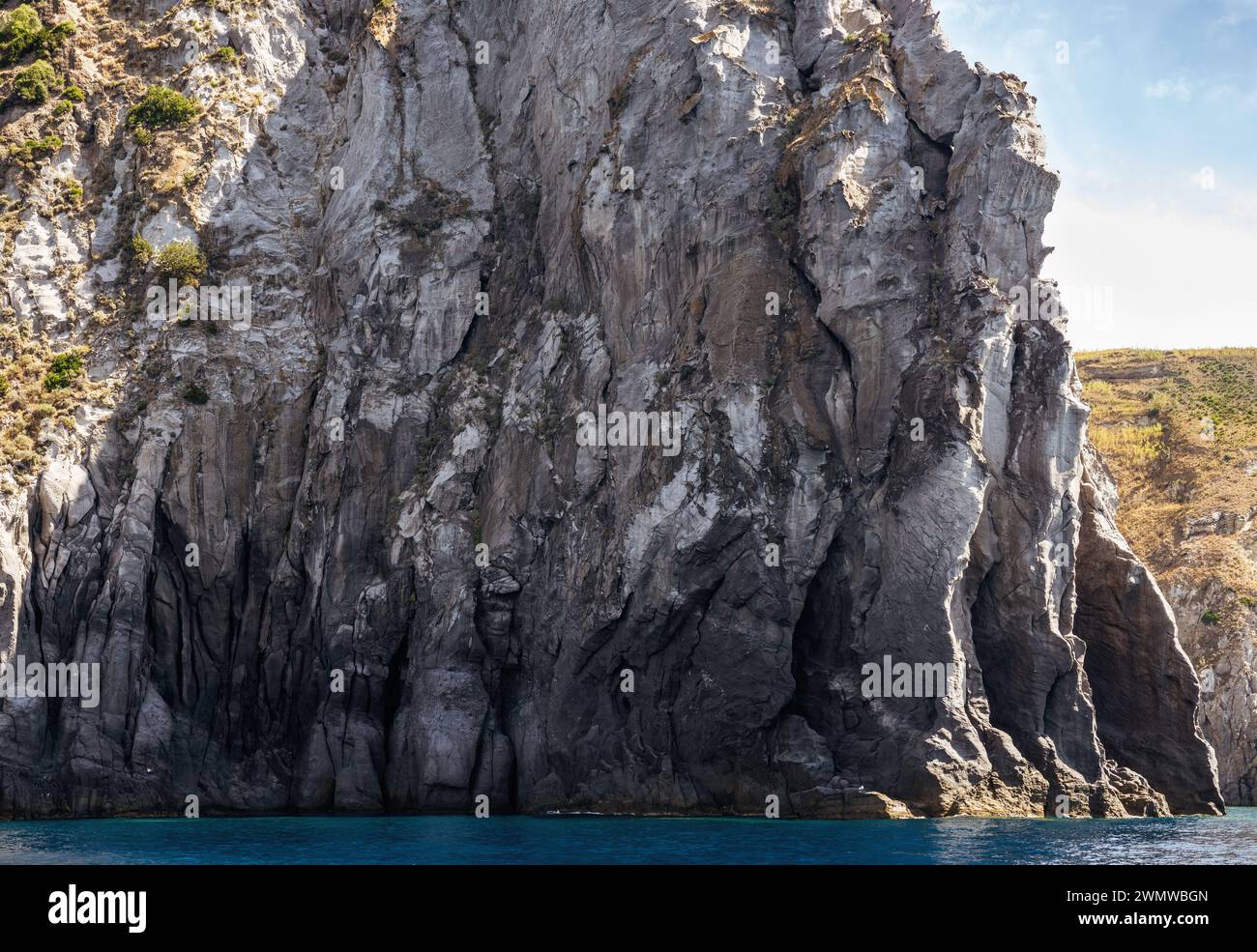 Weathered seaside rock face texture with parts of green and blue water ...