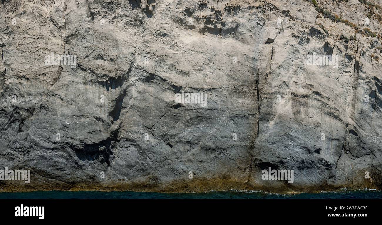 Weathered seaside rock face texture with parts of green and blue water ...