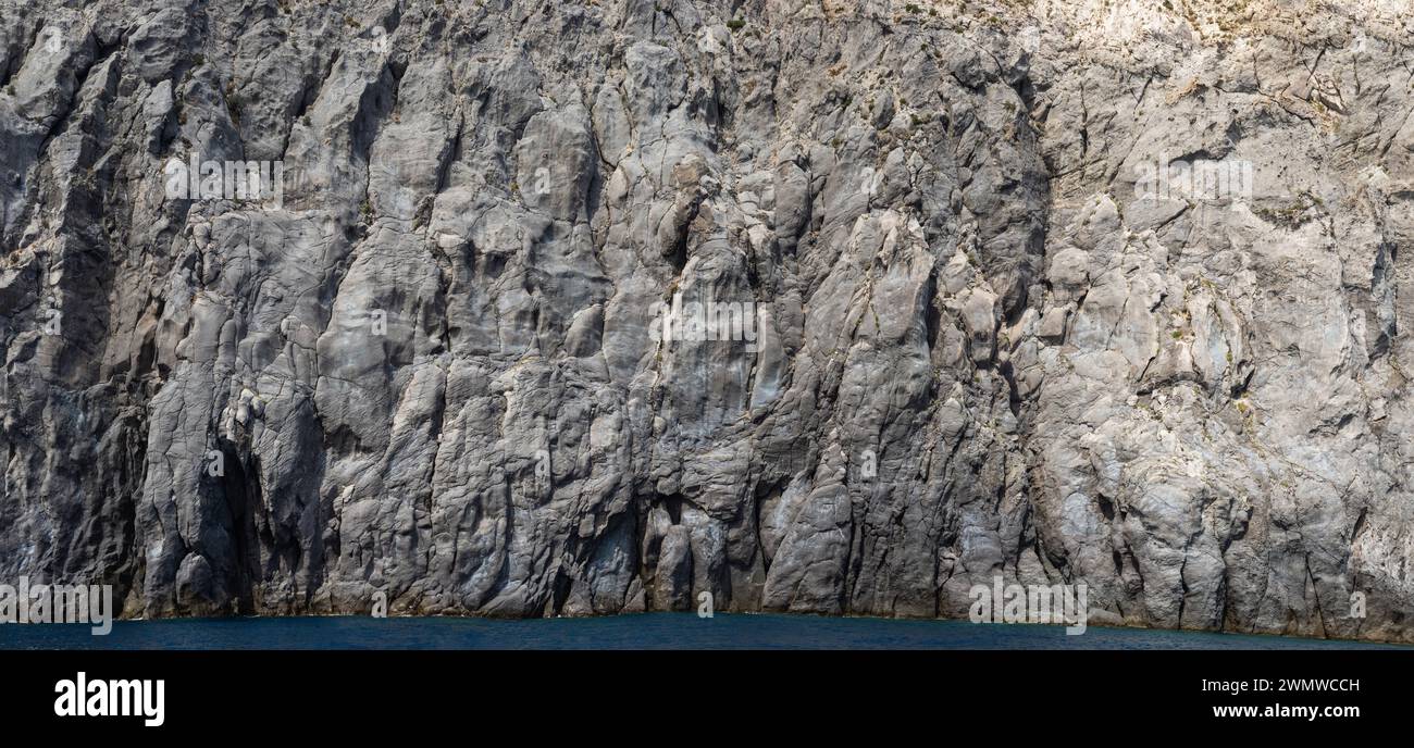 Weathered seaside rock face texture with parts of green and blue water ...