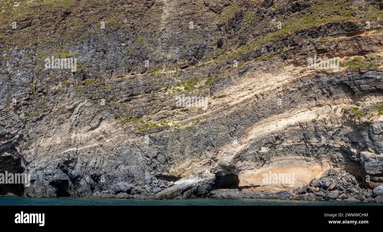 Weathered seaside rock face texture with parts of green and blue water ...