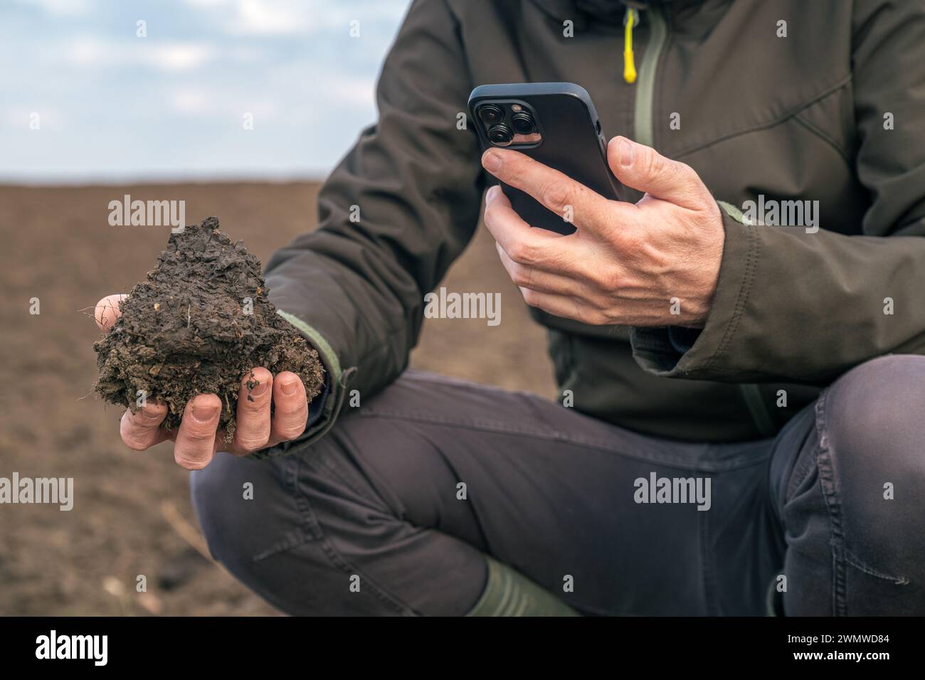 Agronomist is holding a clod of earth and smartphone, using the device ...