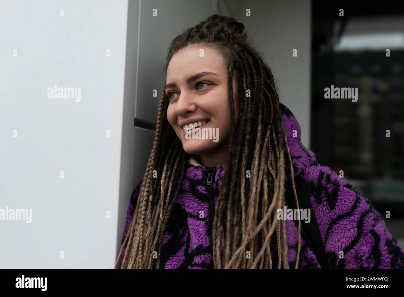 European woman with dreadlocks and piercings wearing a purple jacket ...