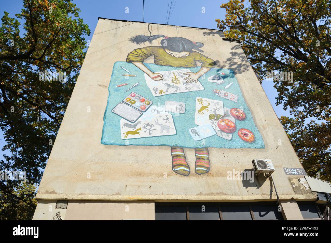 A large mural on the end of an apartment building, depicting a young ...
